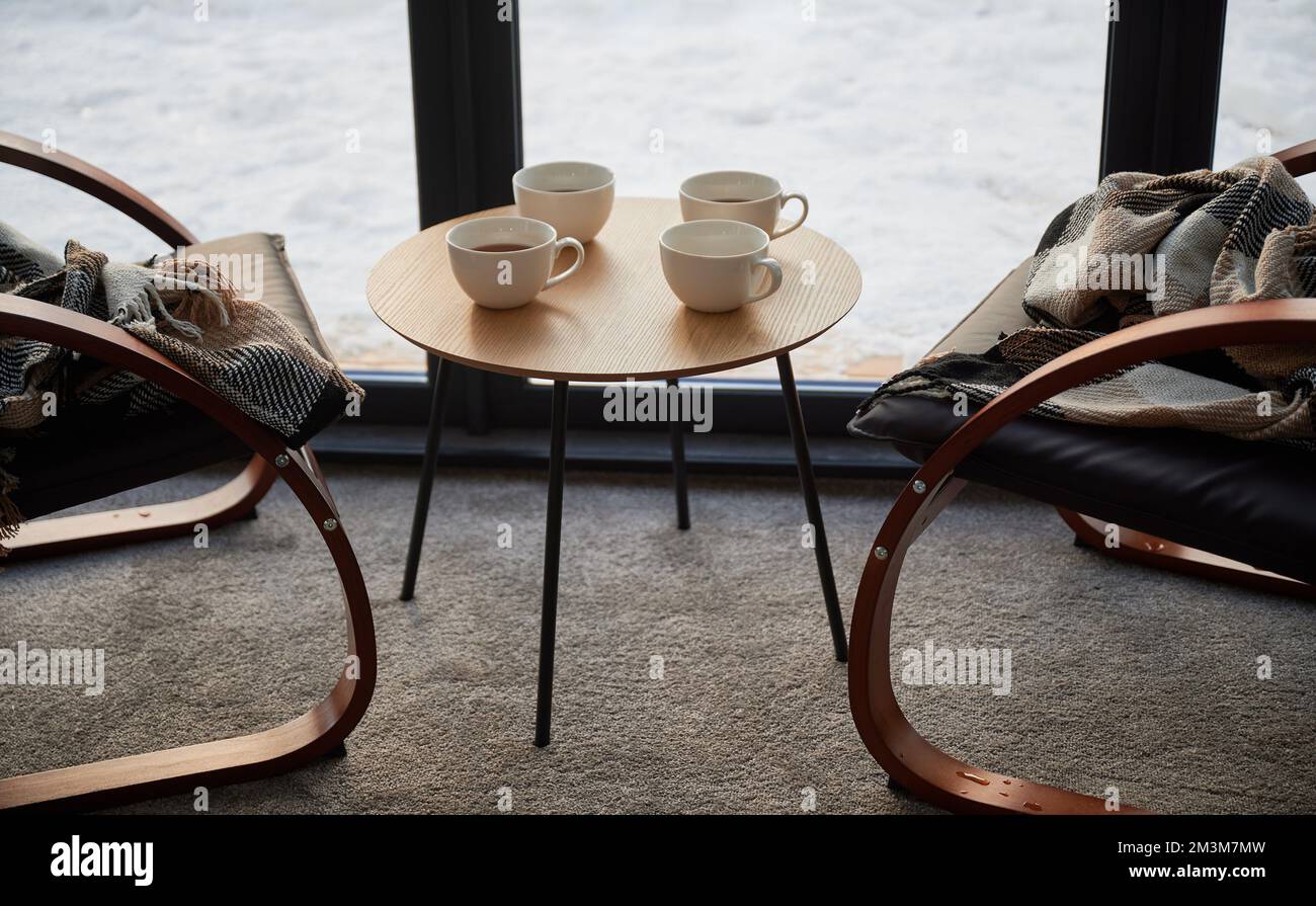 Four cups of unfinished tea on small table and cozy designed chairs ...