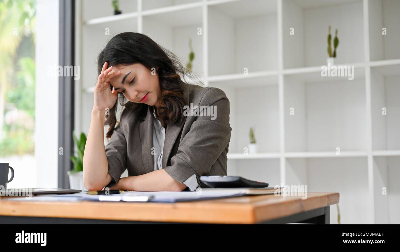 Stressed millennial Asian businesswoman sits at her desk suffering from ...