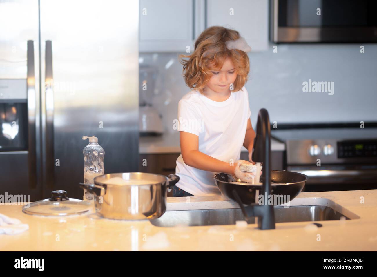 Child help in washing dishes at kitchen. Dishwashing liquid with a ...