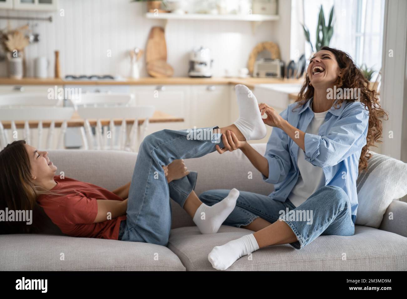 Overjoyed mother laughing out of loud while tickling feet of daughter ...
