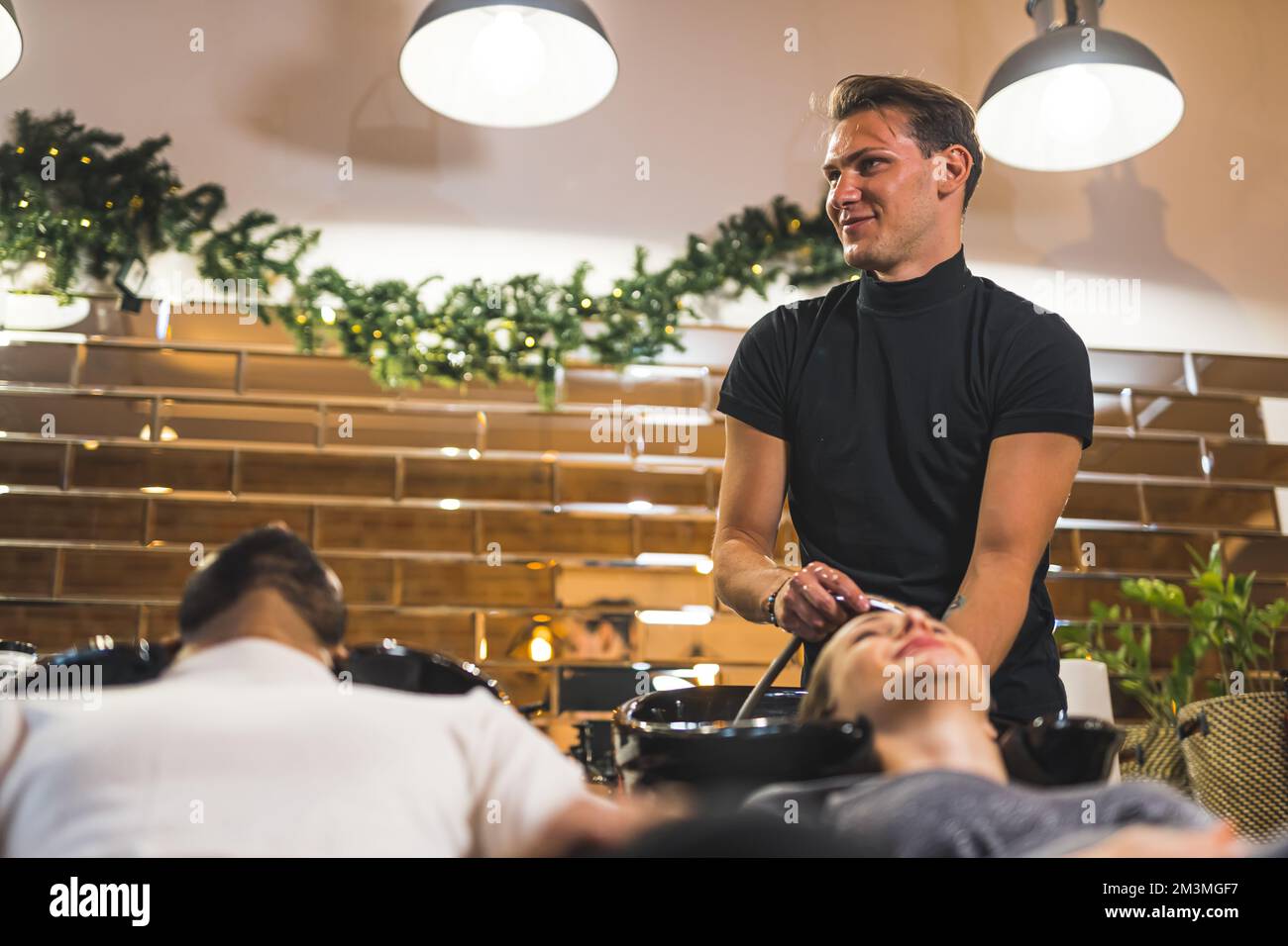 Smiling professional male hairdresser washing his male and female ...