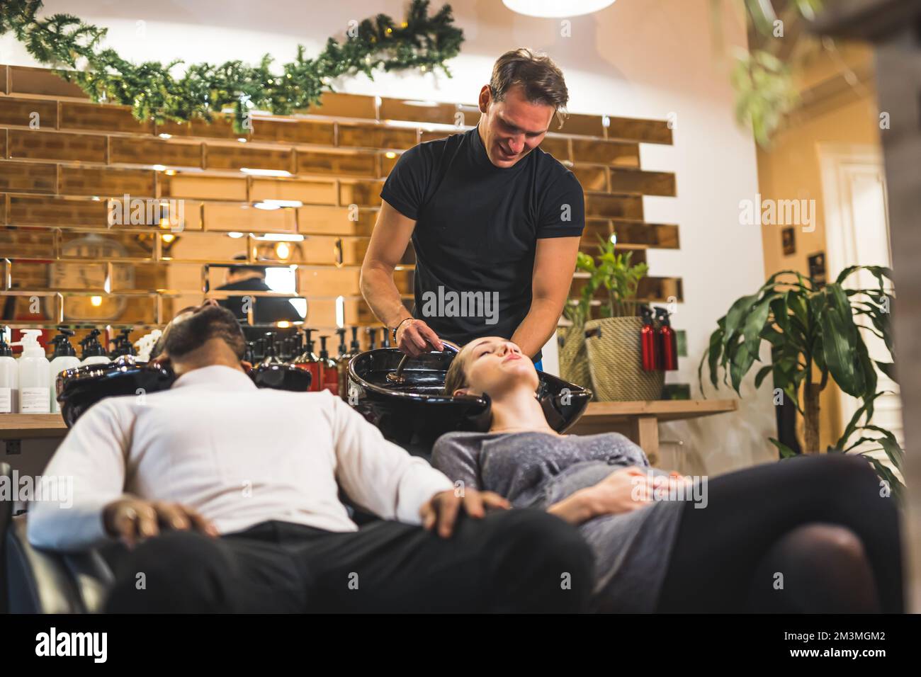 Professional male hairdresser washing his male and female clients hair ...