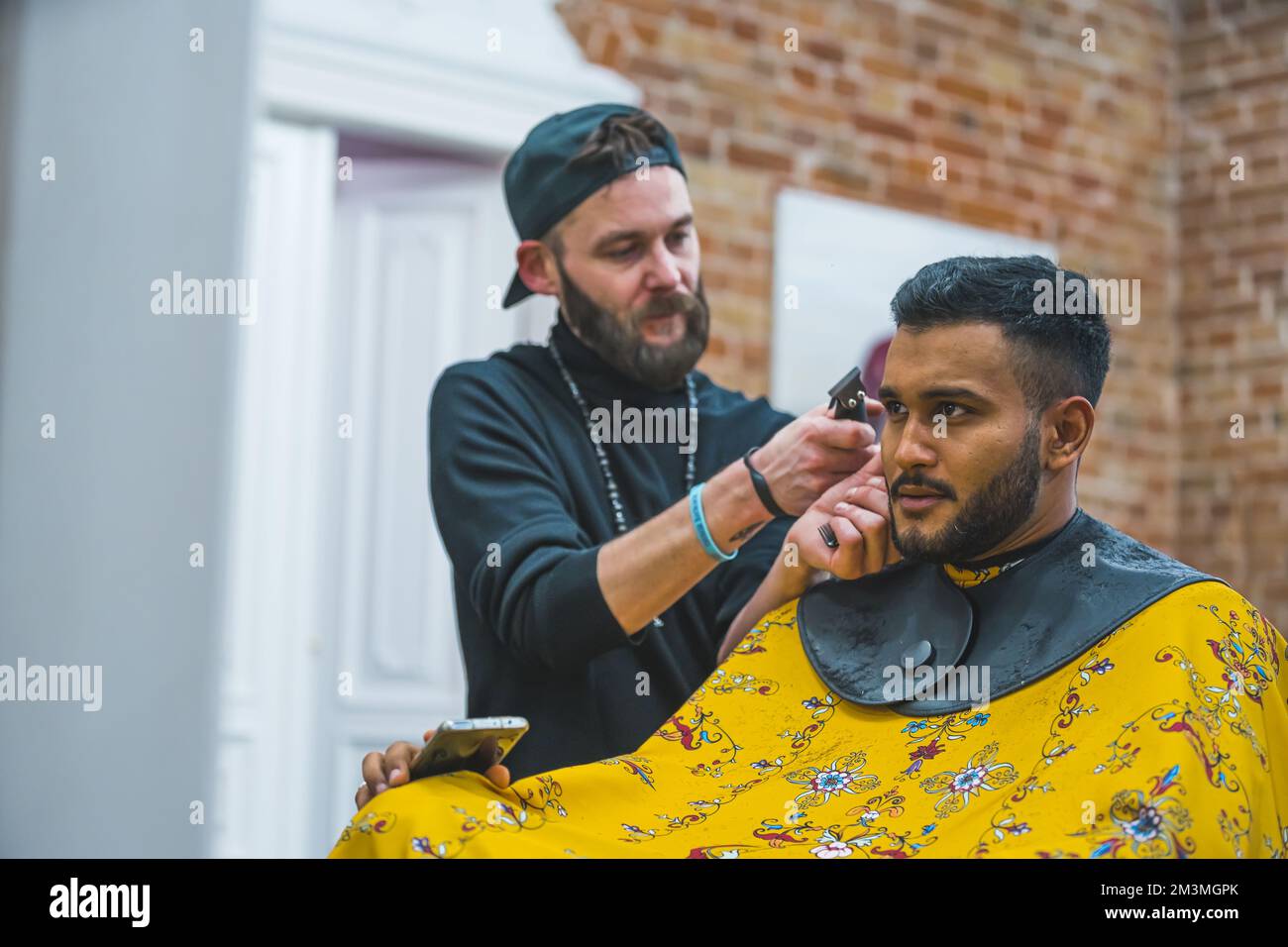 Focus professional barber with black hat trimming his indian client's ...