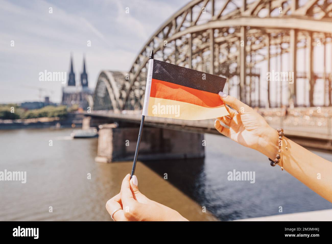 A hand holding a German flag against the Rhine bridge and Cologne Dom ...