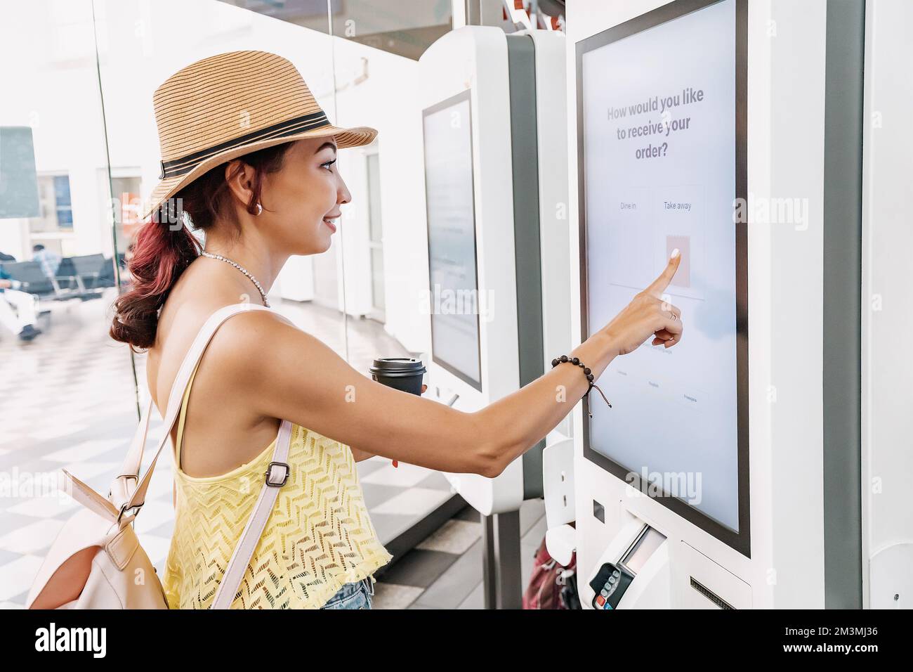 A female customer uses a touchscreen terminal or self-service kiosk to ...