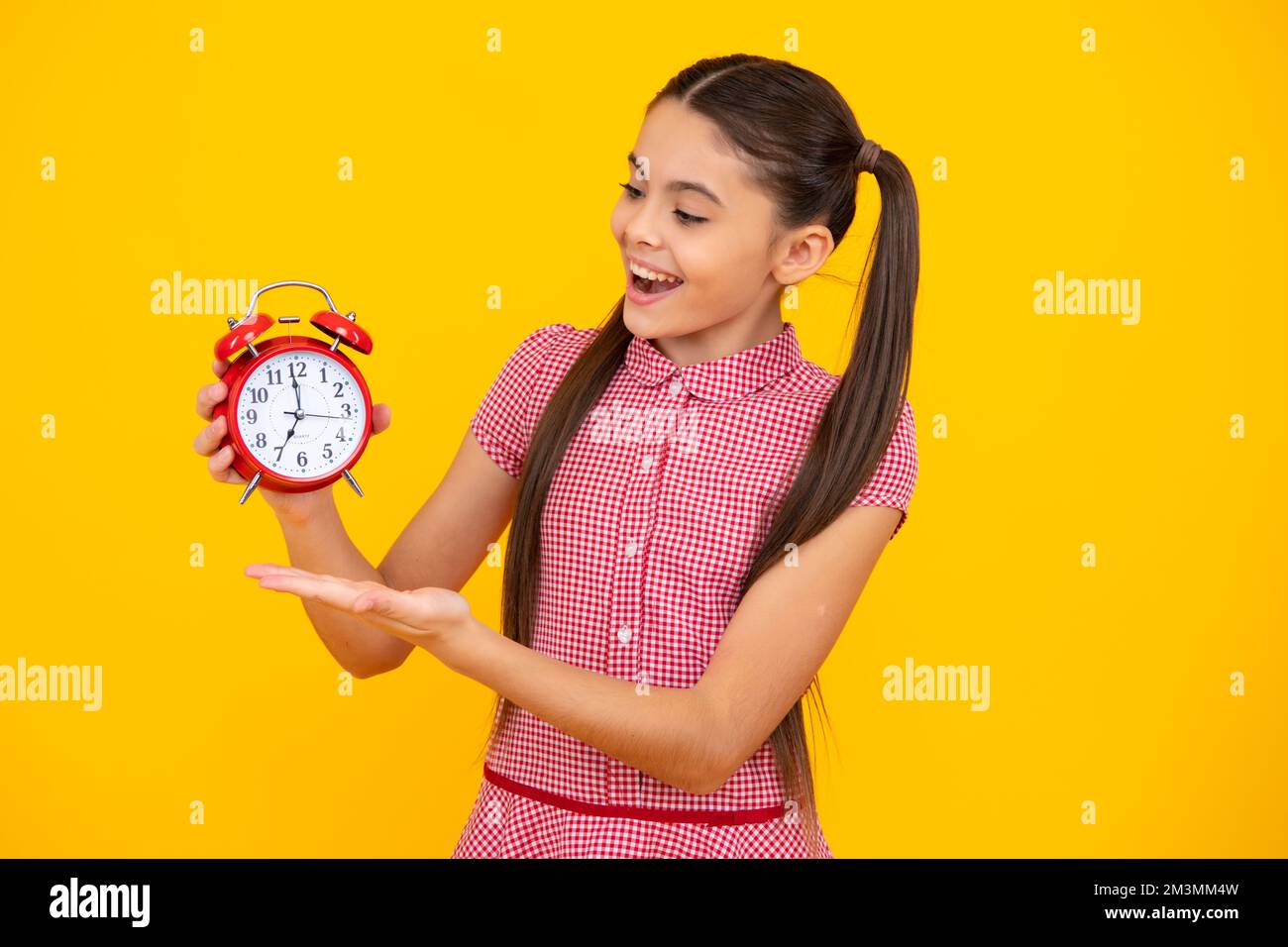 Child teenager girl with alrm clock isolated on yellow background. Time ...
