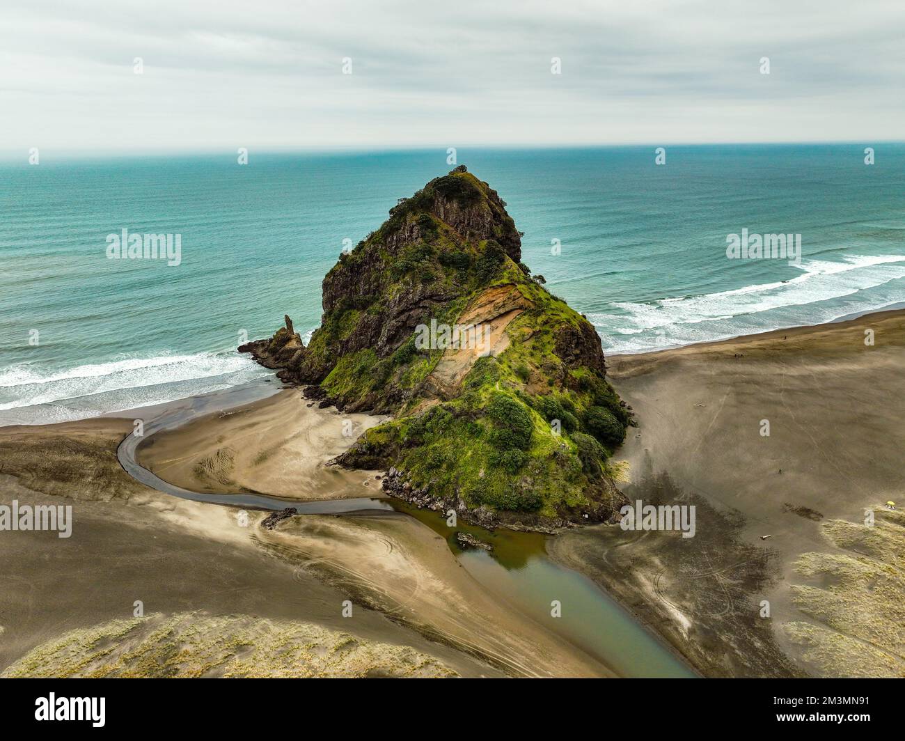 An aerial view of the Lion Rock on Piha Beach with a cloudy sky in the ...