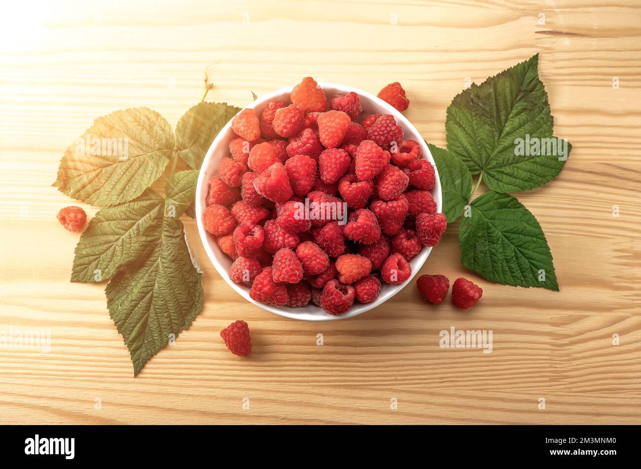 Raspberries on white plate on wooden table with leaves. Organic ...