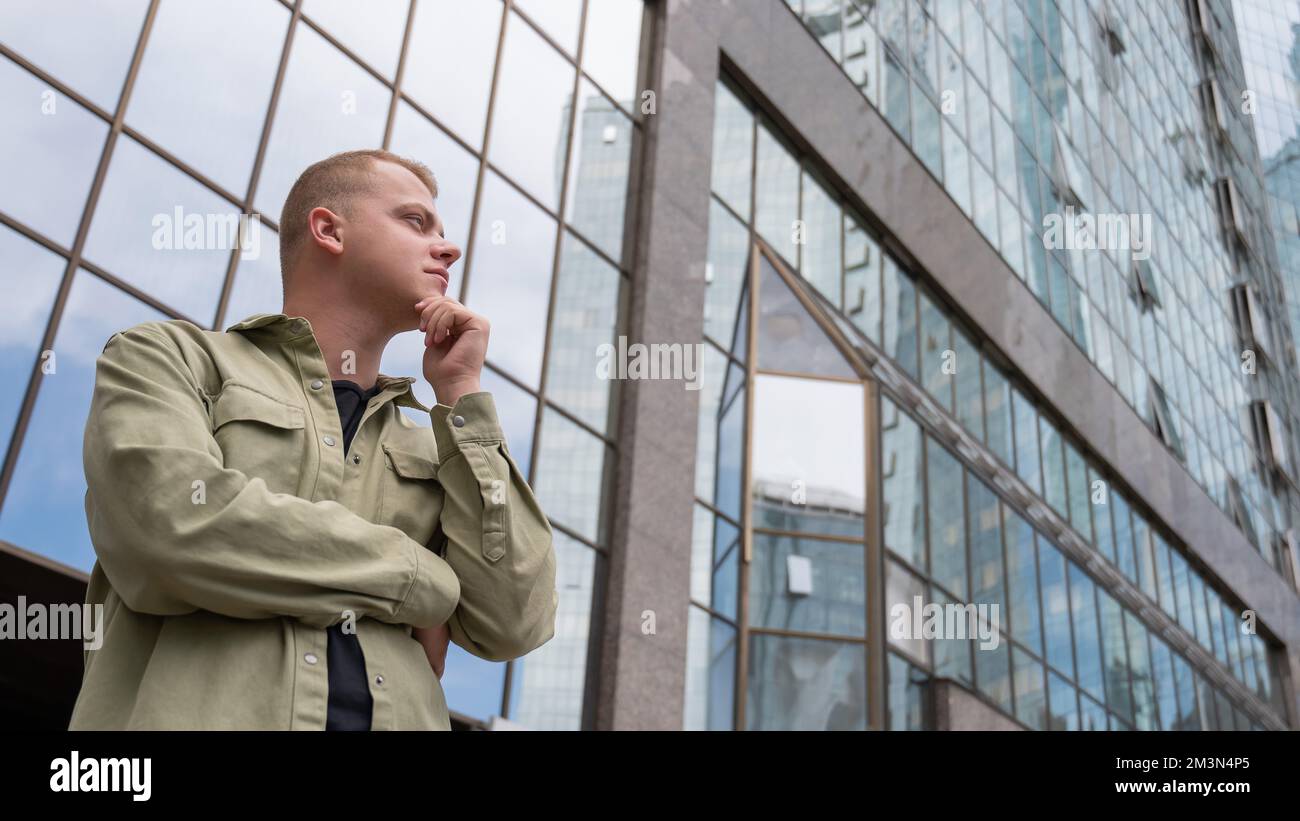A pensive man stands against the backdrop of a skyscraper Stock Photo ...