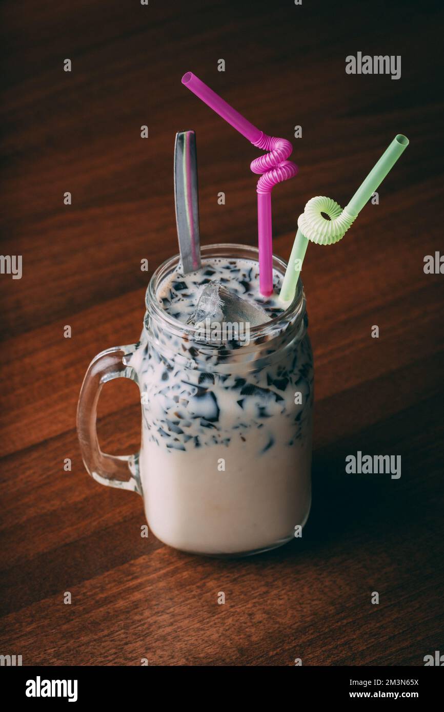 A vertical closeup of a glass of a cold milk tea on a wooden table ...
