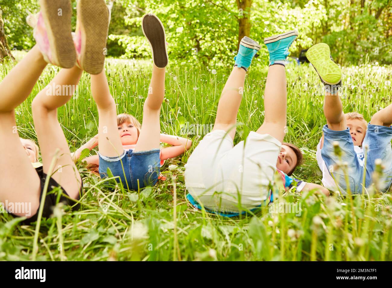 Multiracial boys and girls with legs up lying down in meadow during ...