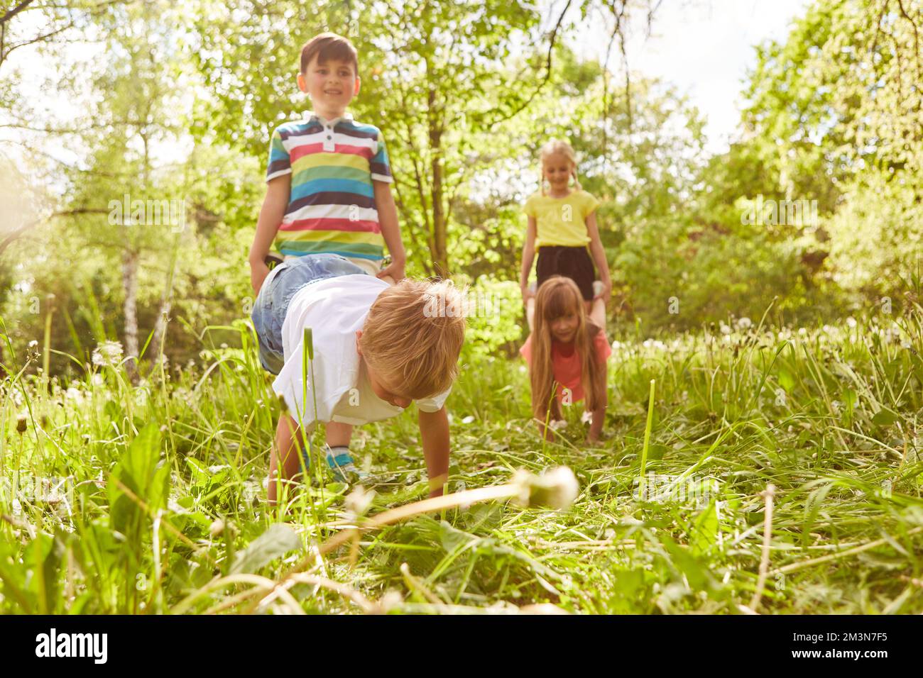 Playful boys and girls competing each other in meadow on sunny day ...