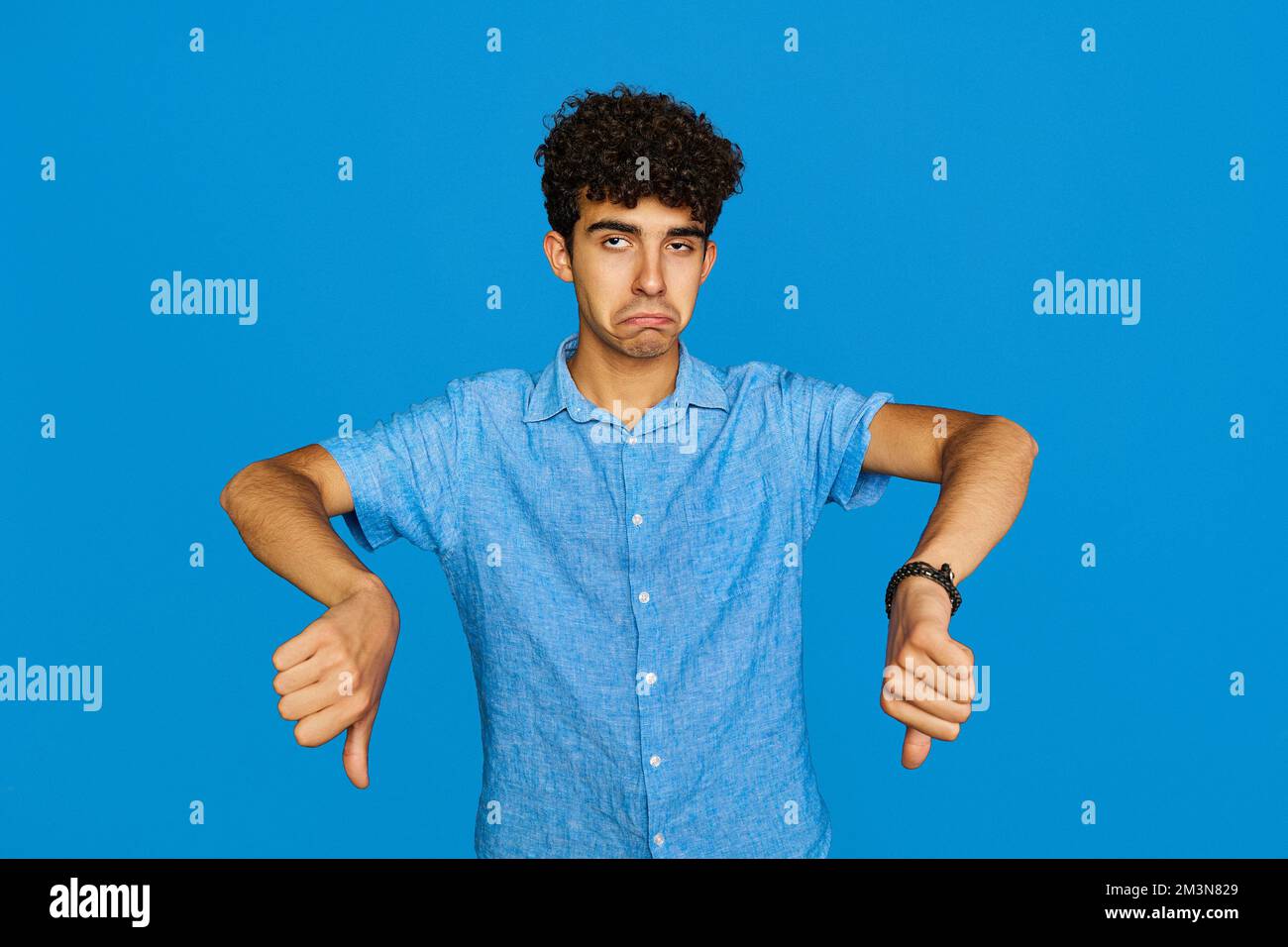 Upset teenage boy with casual clothes and wavy black hair frowning ...