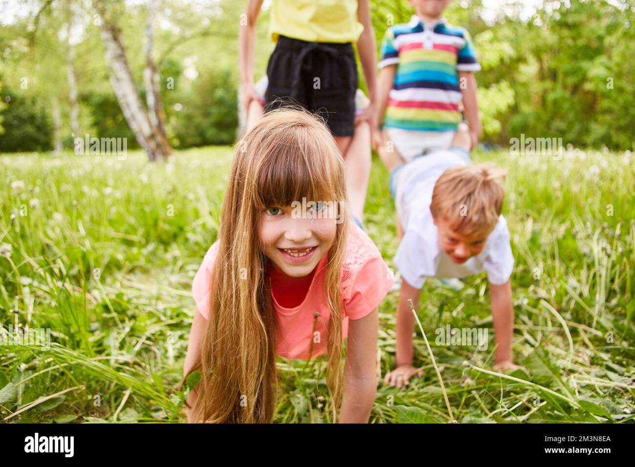 Portrait of playful girl playing with friends during wheelbarrow race ...