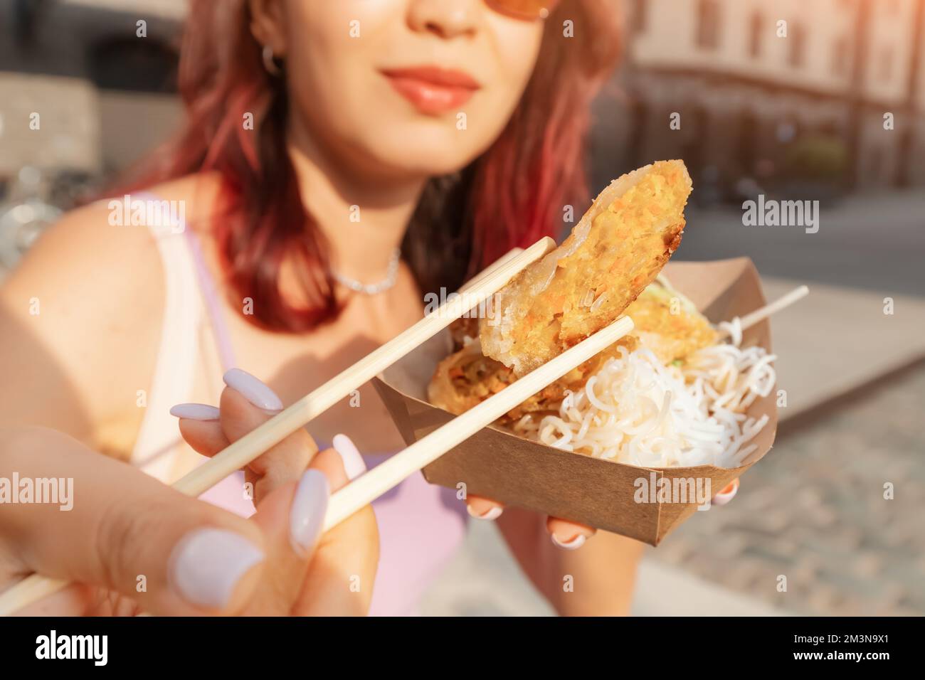Happy cheerful girl eating spring rolls from takeaway paper box using ...