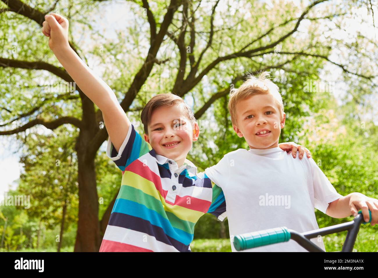 Portrait of happy boy and friend with bicycles standing in park during ...