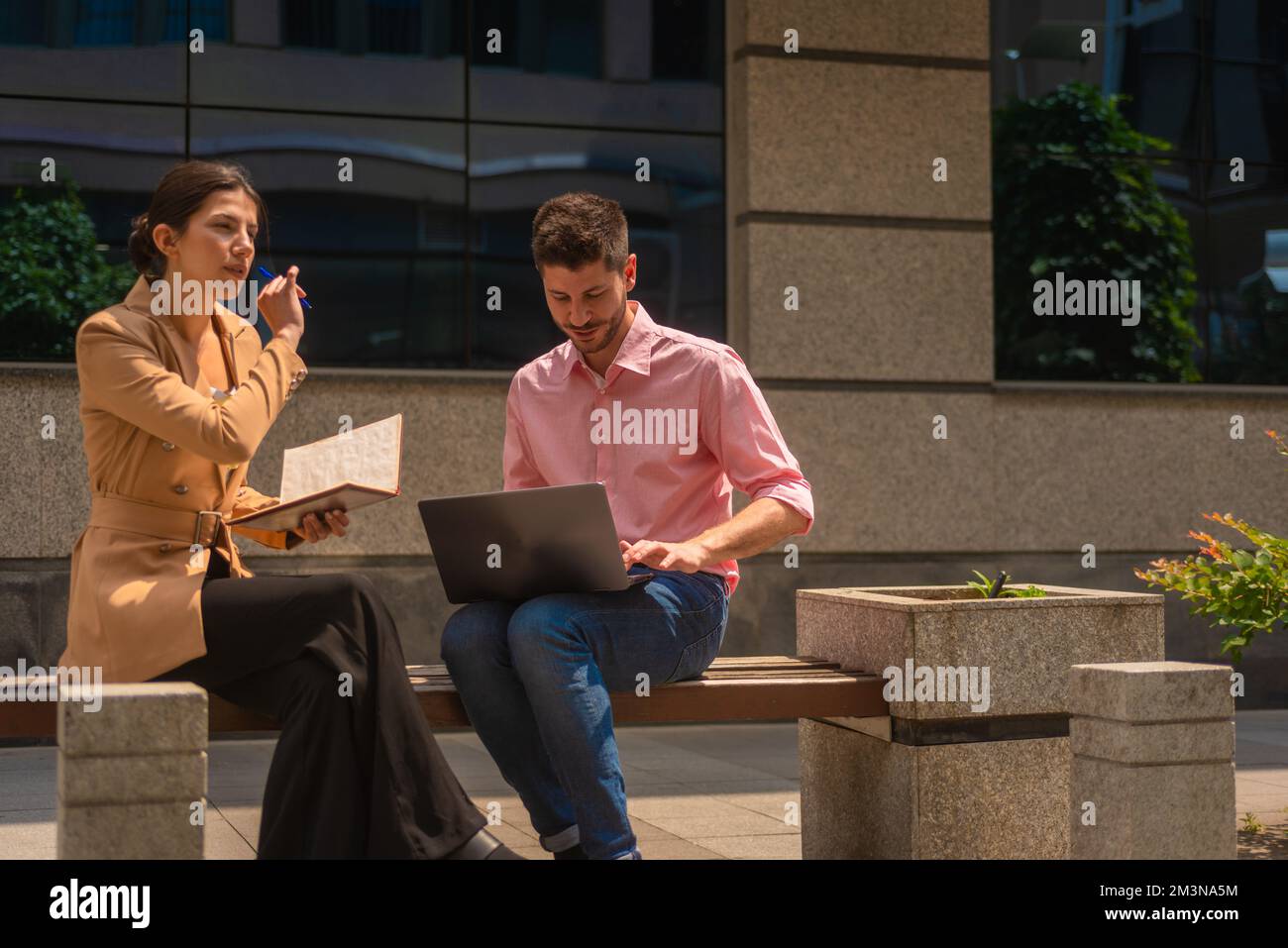 Two business people are sitting on a bench and trying to find a ...