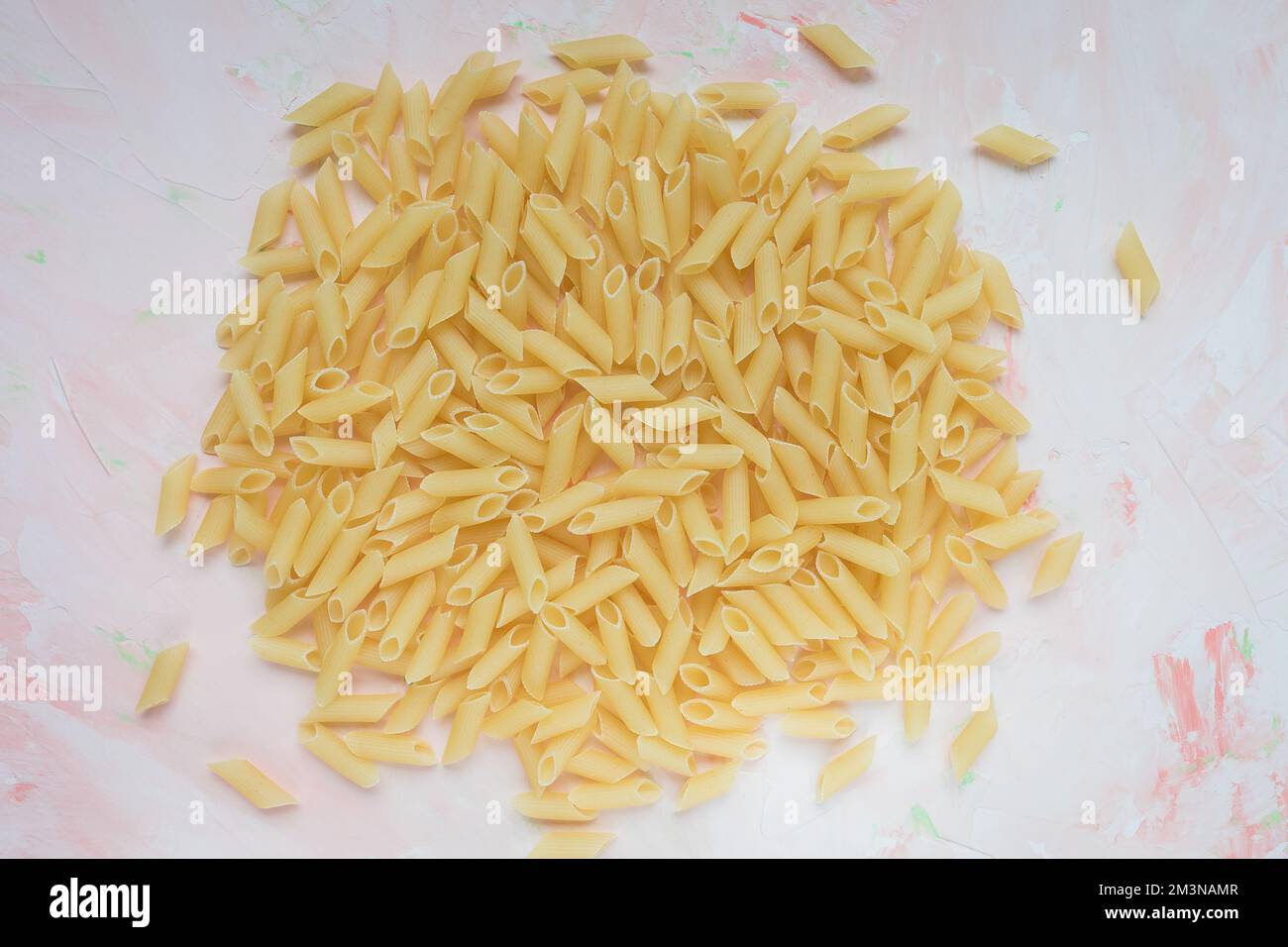 Pile of raw traditional Italian penne pasta on piink background ...
