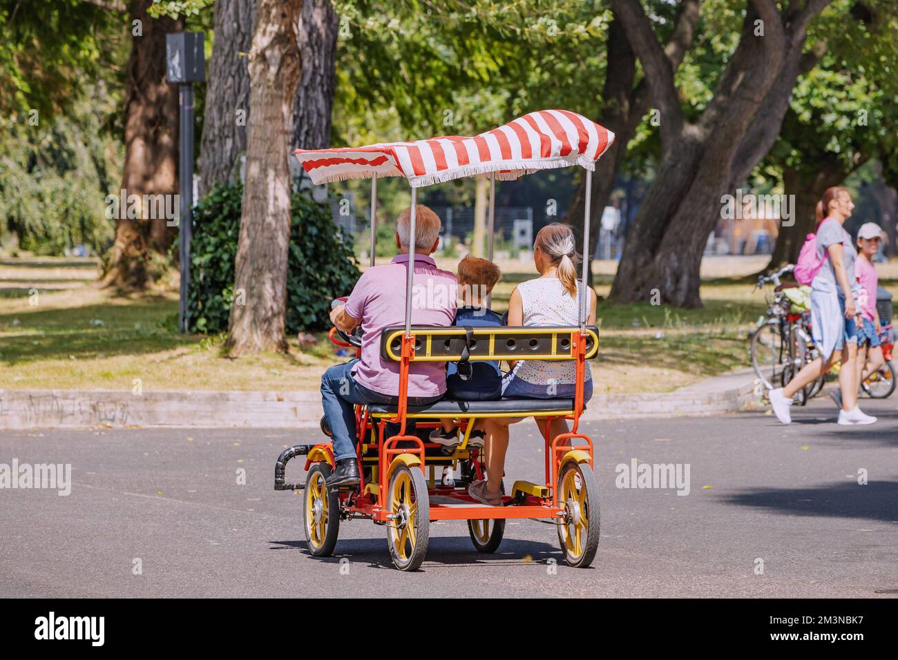 30 July 2022, Cologne, Germany: Family having a relax leisure ride on a four-wheeled bicycle or ...