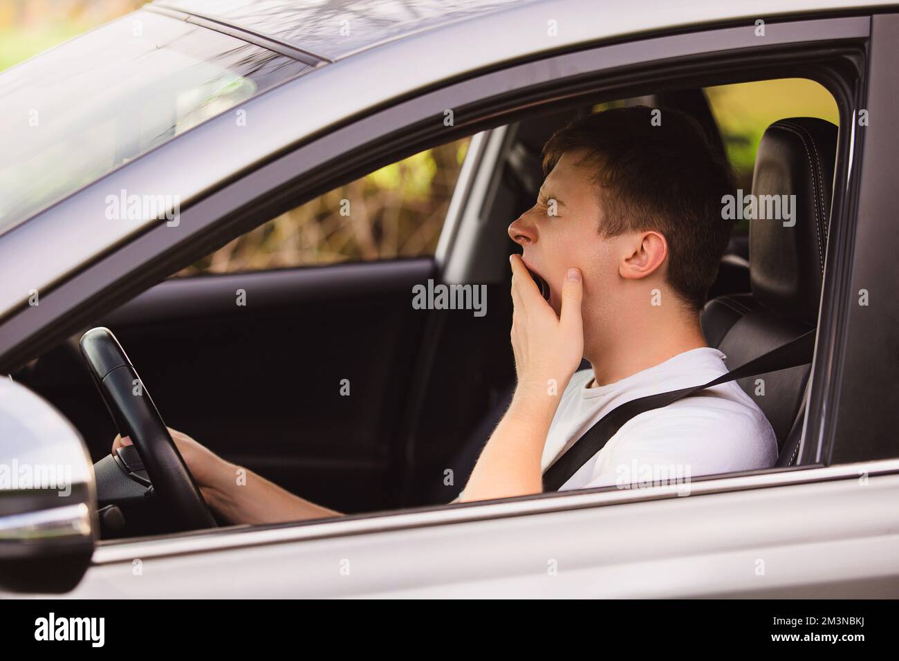 Tired novice driver yawning while driving his car. Exhausted young guy ...