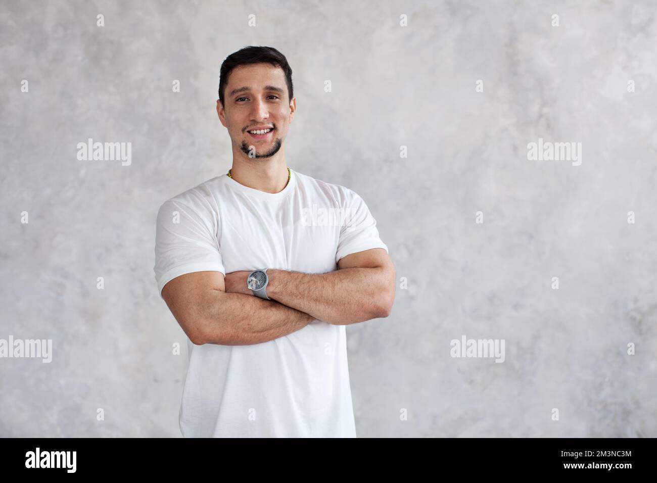 Brunette man smiles, looks at camera, crossed arms over chest on white ...