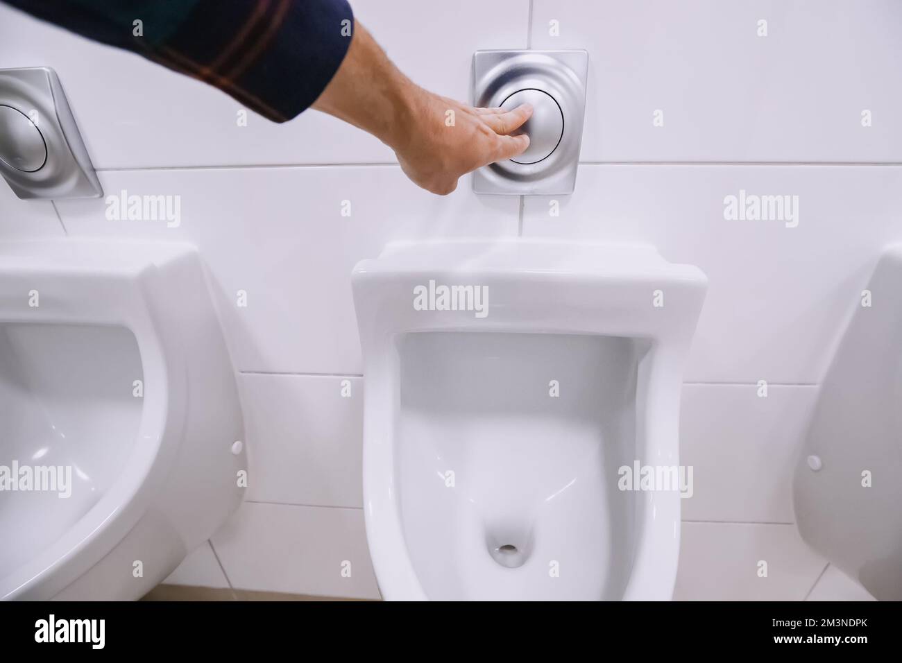 Male hand flashing water in urinals in a public men's toilet. The ...