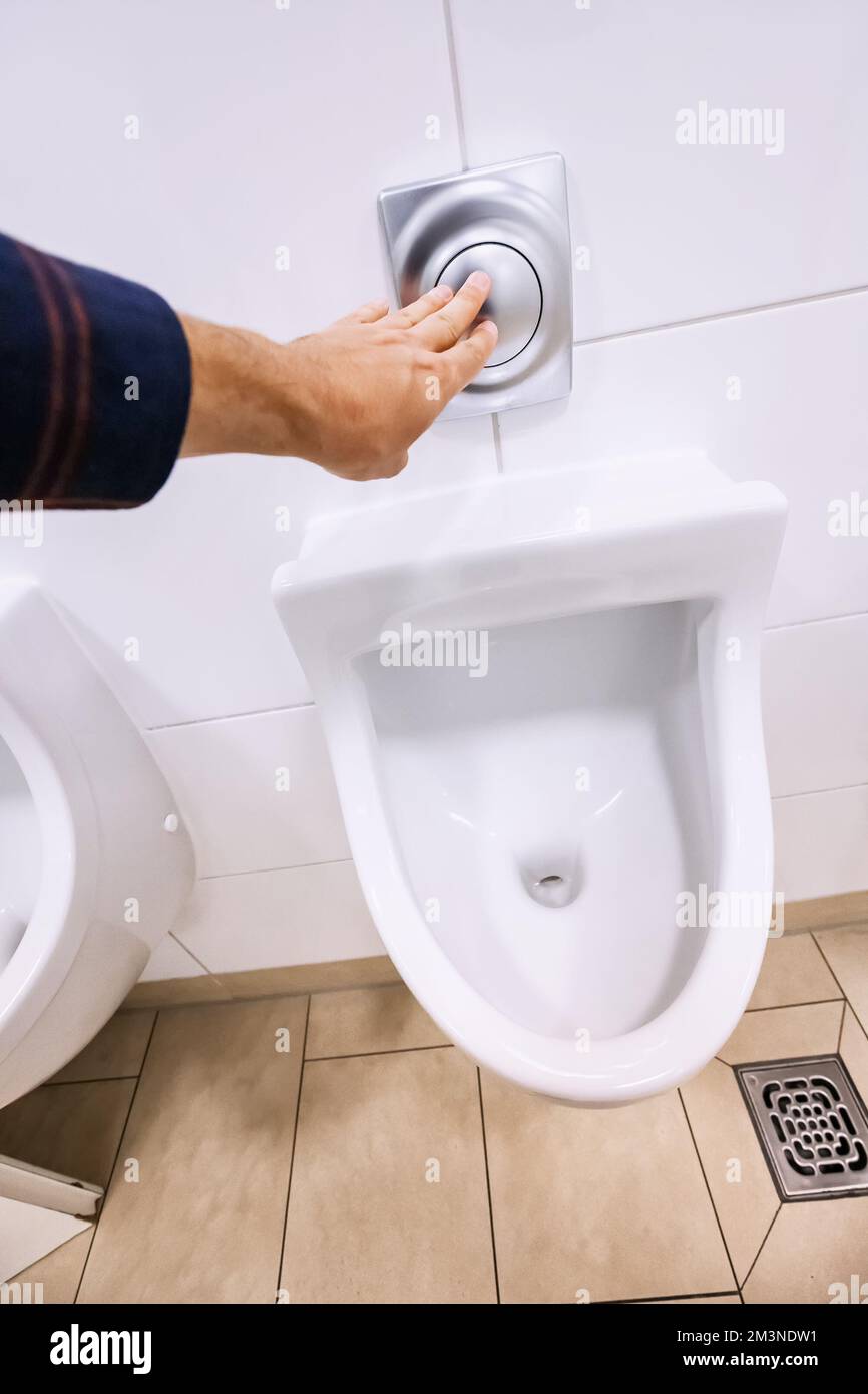 Male hand flashing water in urinals in a public men's toilet. The ...