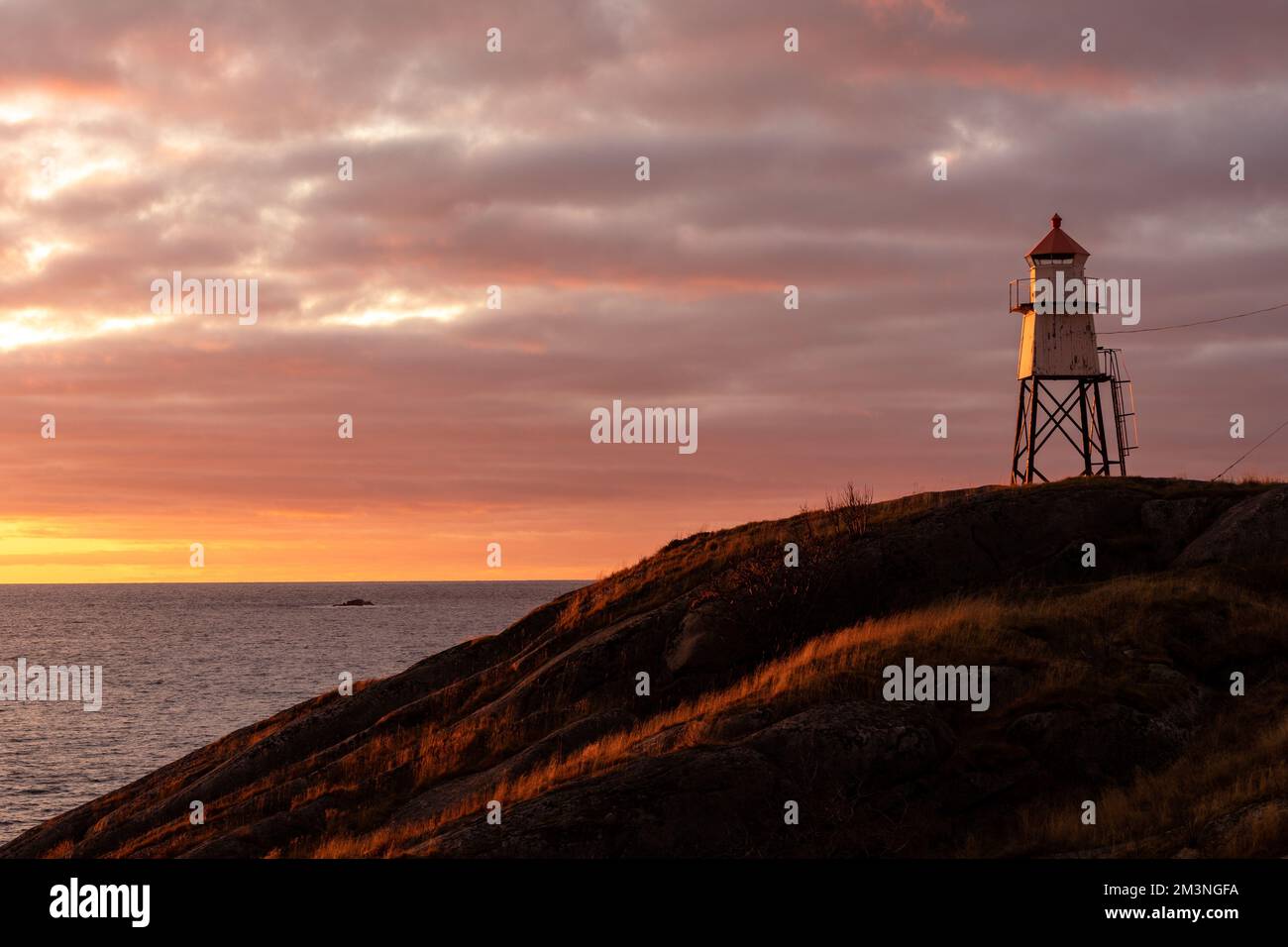 A beautiful sunset over the lighthouse on the hill in Henningsvaer ...