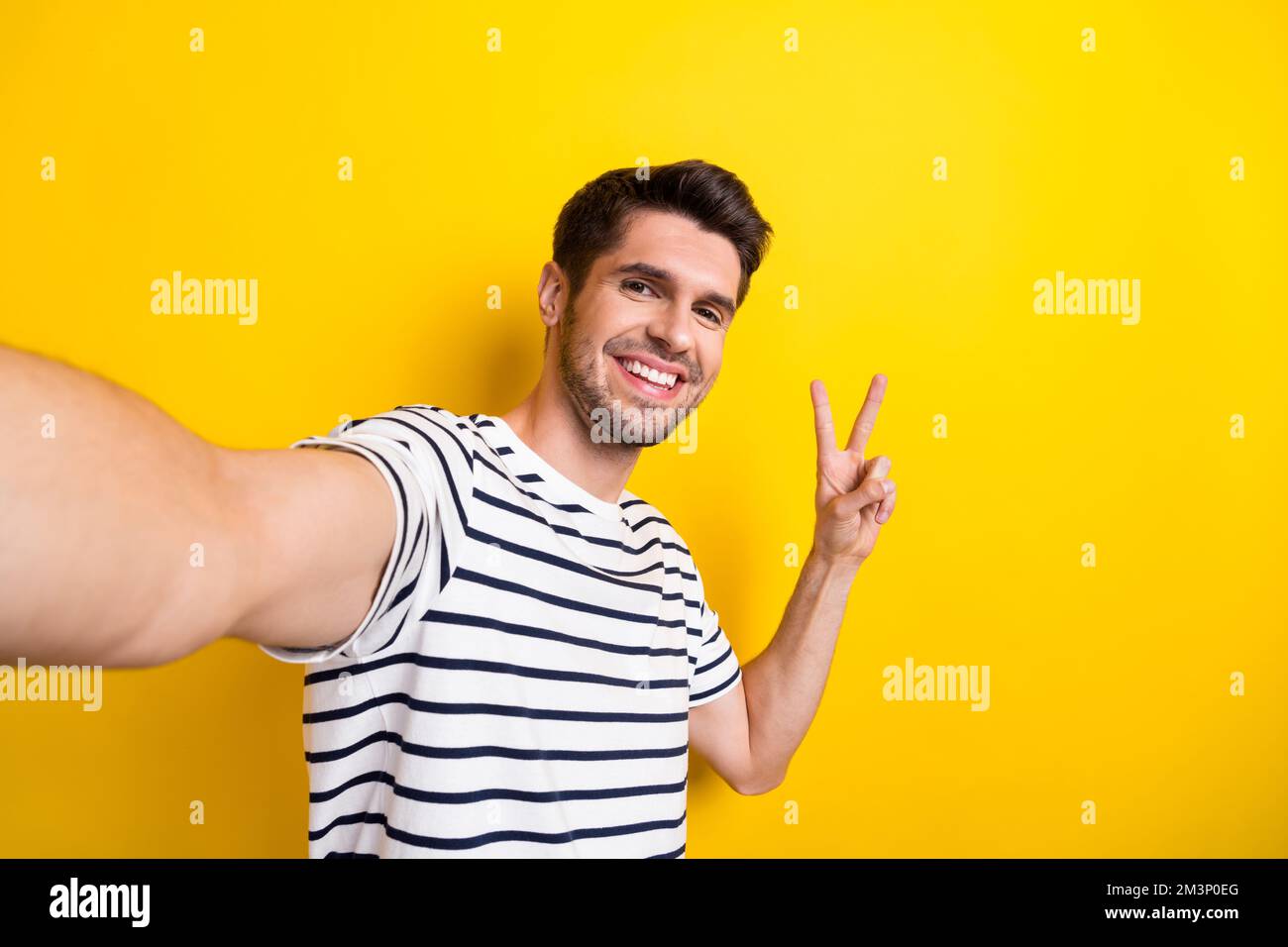 Portrait of nice satisfied young man take selfie demonstrate v-sign isolated on yellow color ...
