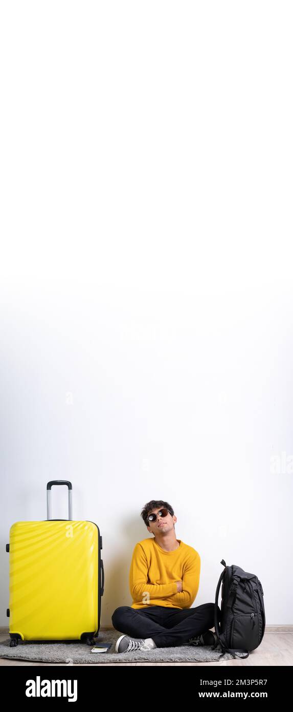 A bored tourist traveler with a suitcase sits and dreams on a white ...