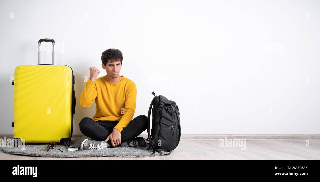 Young traveler man wearing sweater sitting with suitcase over isolated ...
