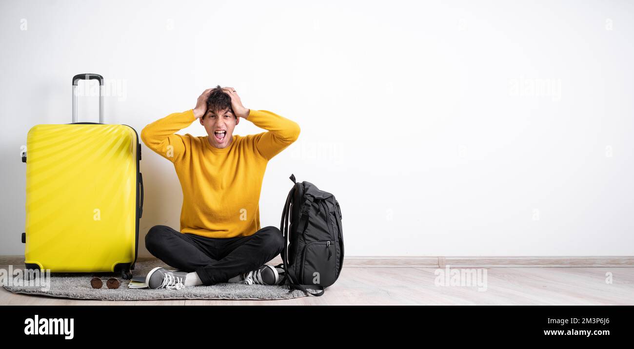 Angry traveler man with suitcase screaming and holding head with hands ...