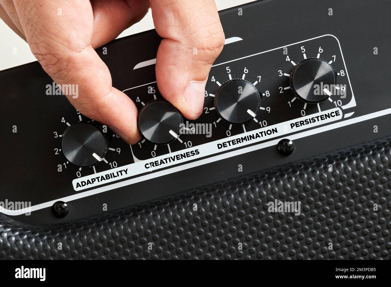 Hand boosting the amplifier knobs with the words creativeness, adaptability, determination and ...