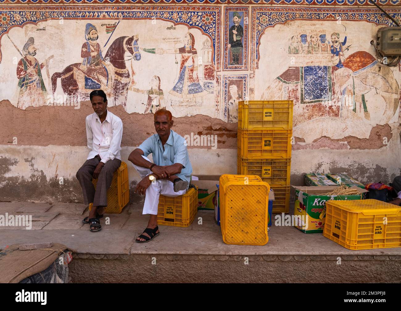 Indian men sit in front of an old mural depicting horses and elephants ...