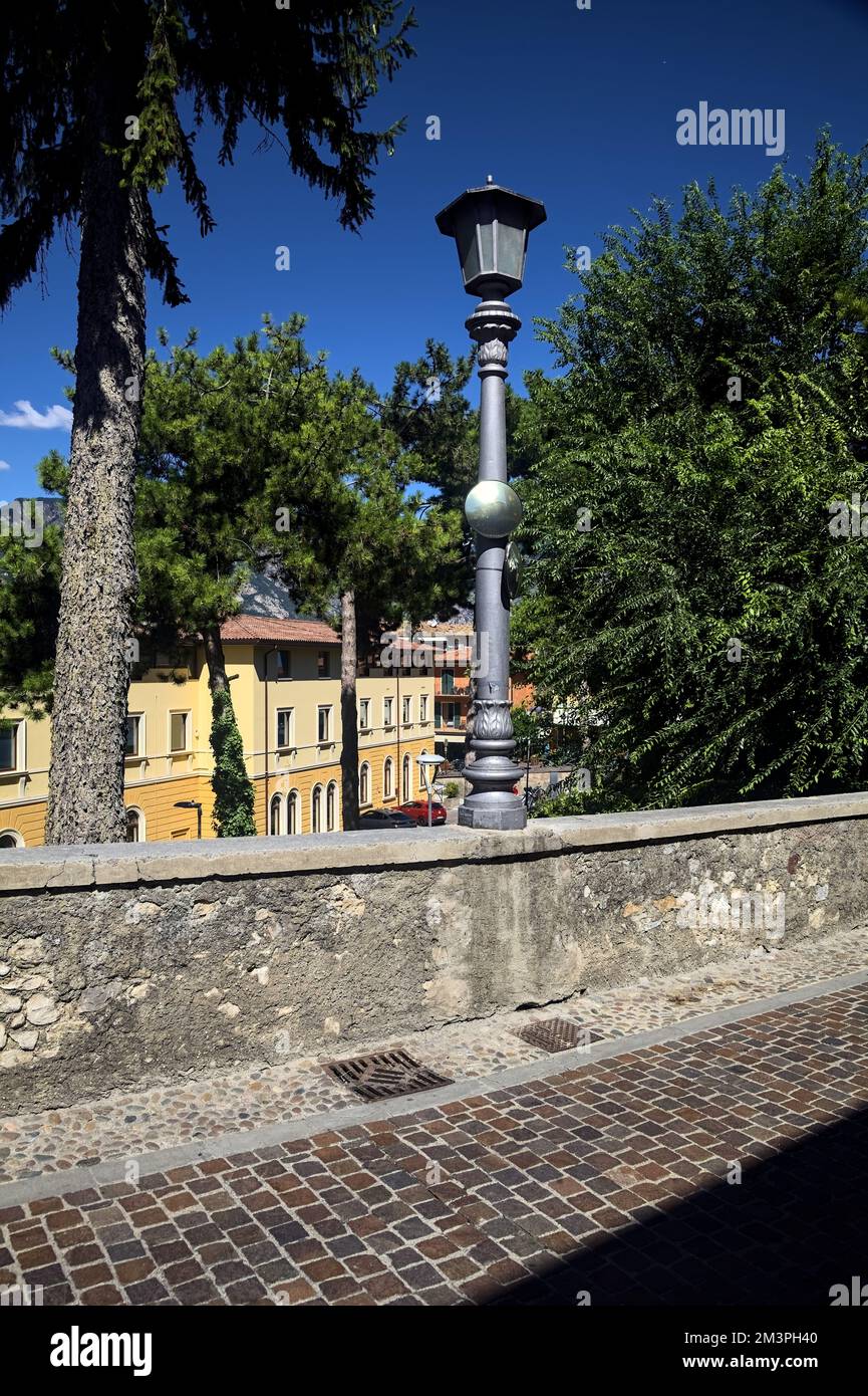Street lamp on a stone wall by the edge of an alley next to tree tops ...