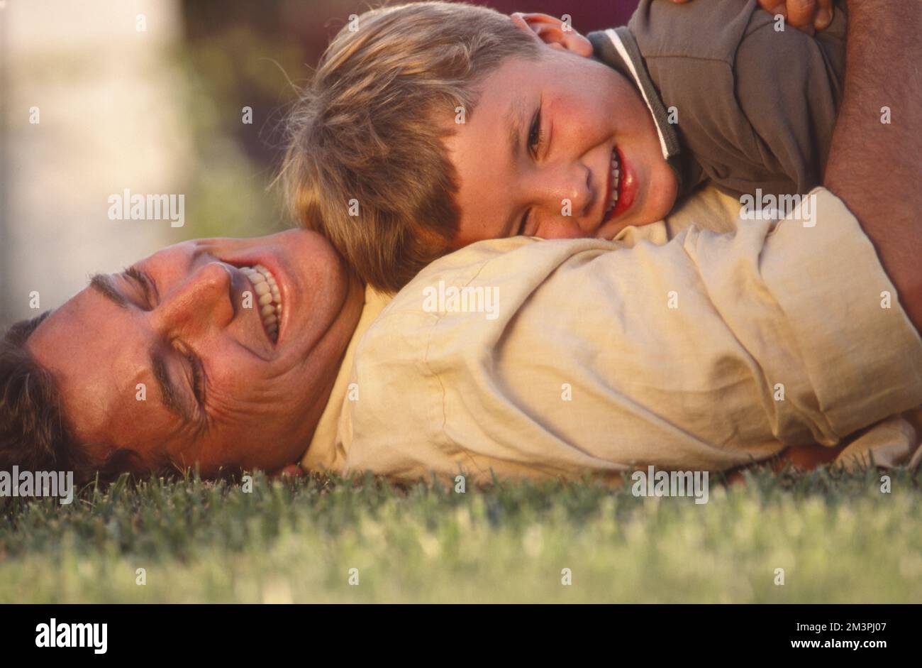 Young boy laying on top of his father while laying in the grass Stock ...