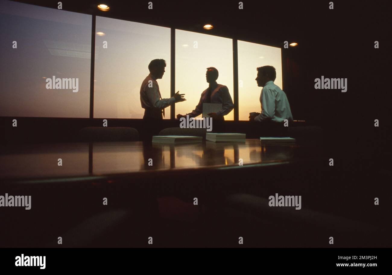 Silhouette image of a group of 3 businessmen sitting in front of a ...