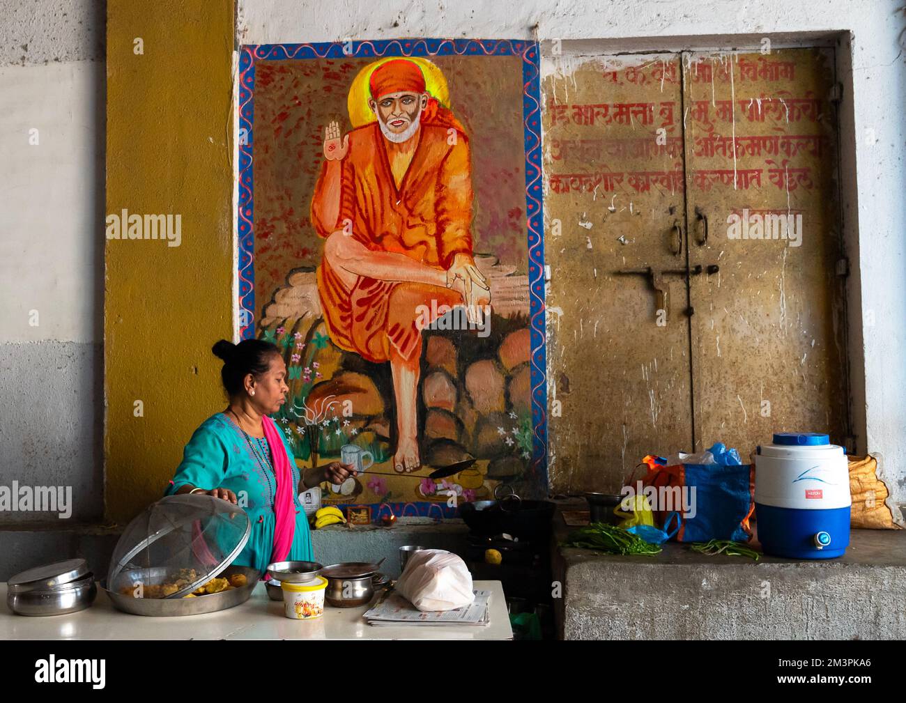 Indian woman preparing food in the street under a guru mural ...