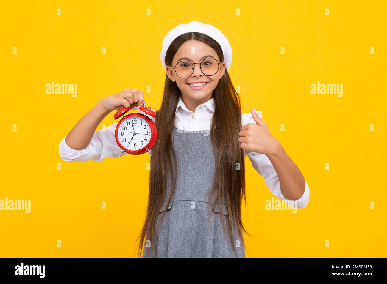 Teenager child hold clock isolated on yellow studio background ...