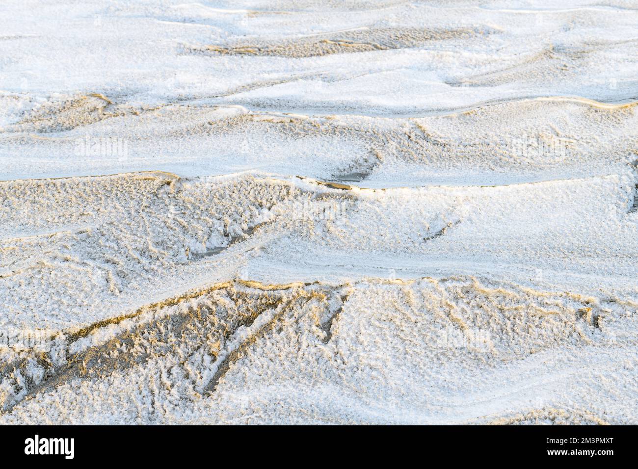 Pattern of snow covered ripples in the sand on the beach, lit by the ...