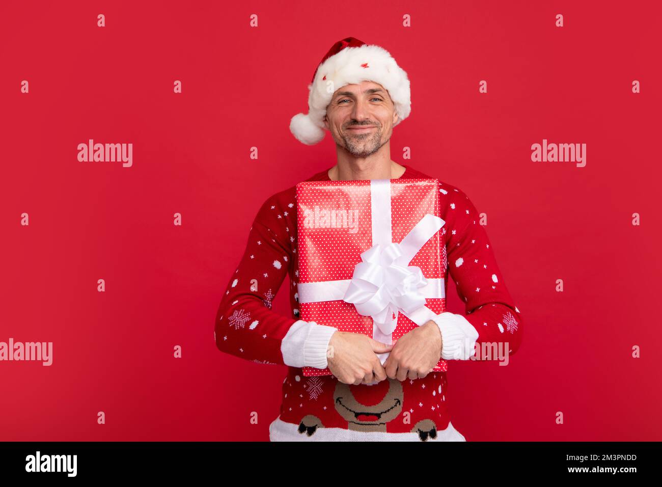 Christmas gift. Man in holiday sweater and Santa hat on studio ...