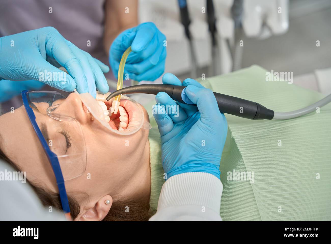Dentist carrying out teeth-whitening procedure on client assisted by ...