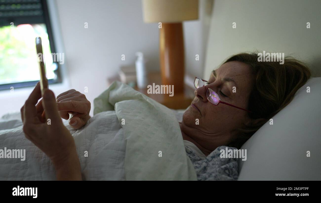 An older woman lying in bed looking at cellphone device a senior person ...