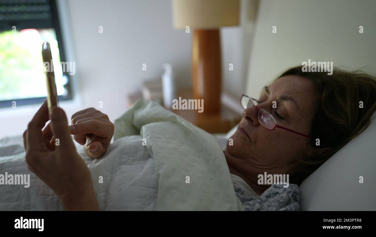 An older woman lying in bed looking at cellphone device a senior person ...