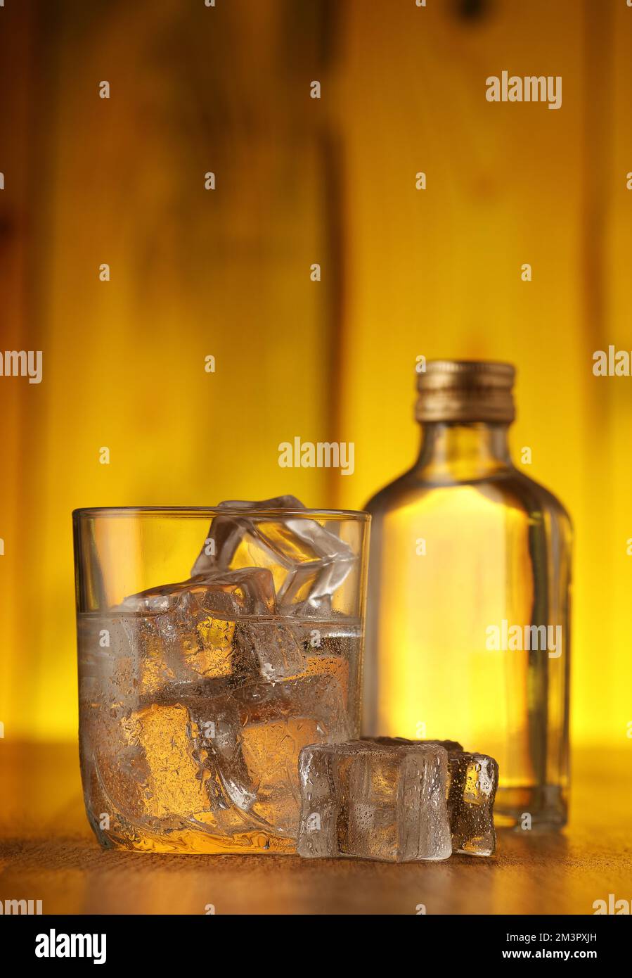 a glass full of liquid with ice cubes and a small bottle of vodka in ...