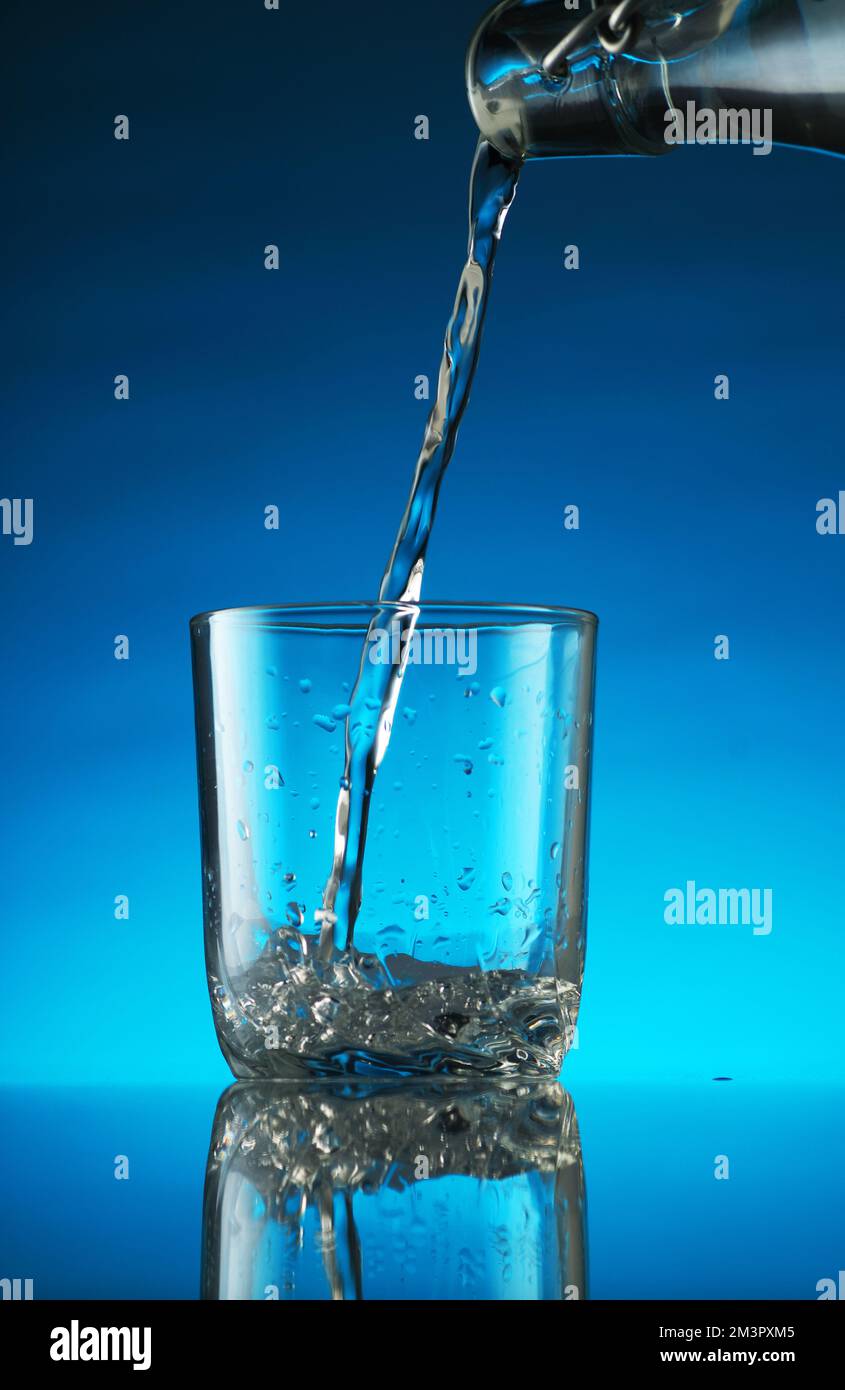 pouring water into a glass on a blue background Stock Photo - Alamy