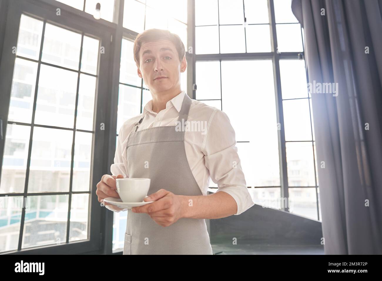 A waiter with a thoughtful look in a gray apron holds out a cup of ...