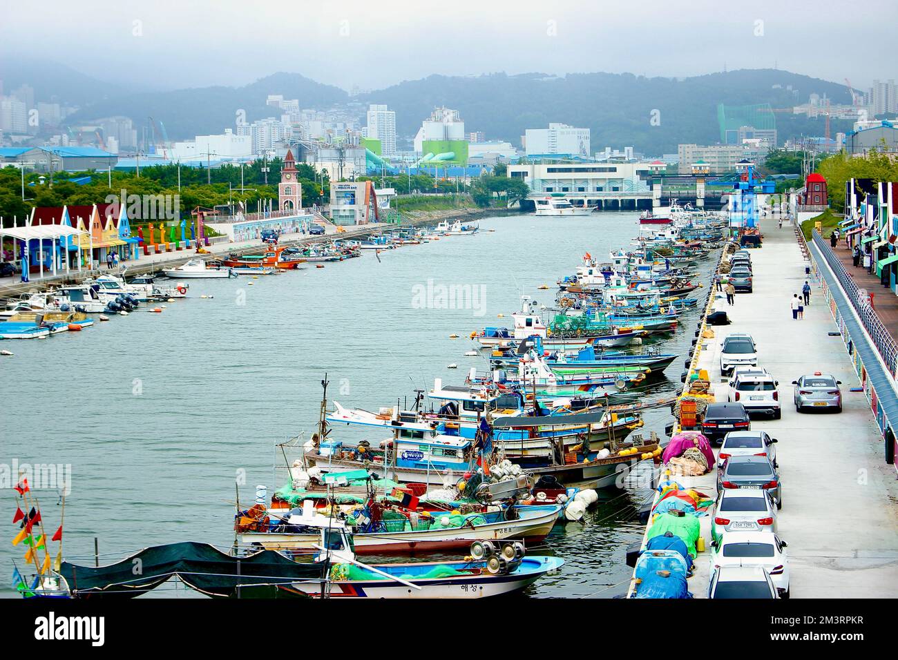 A harbor with colorful fishing boats and cars in the city of Busan ...