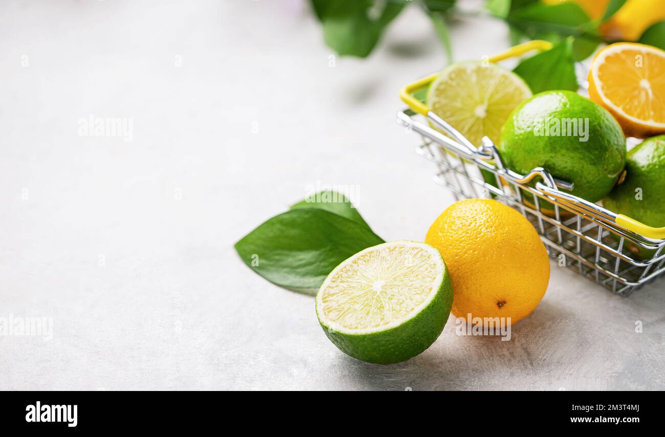 Fresh lemons and limes with leaves in a supermarket basket on a light textured background close ...
