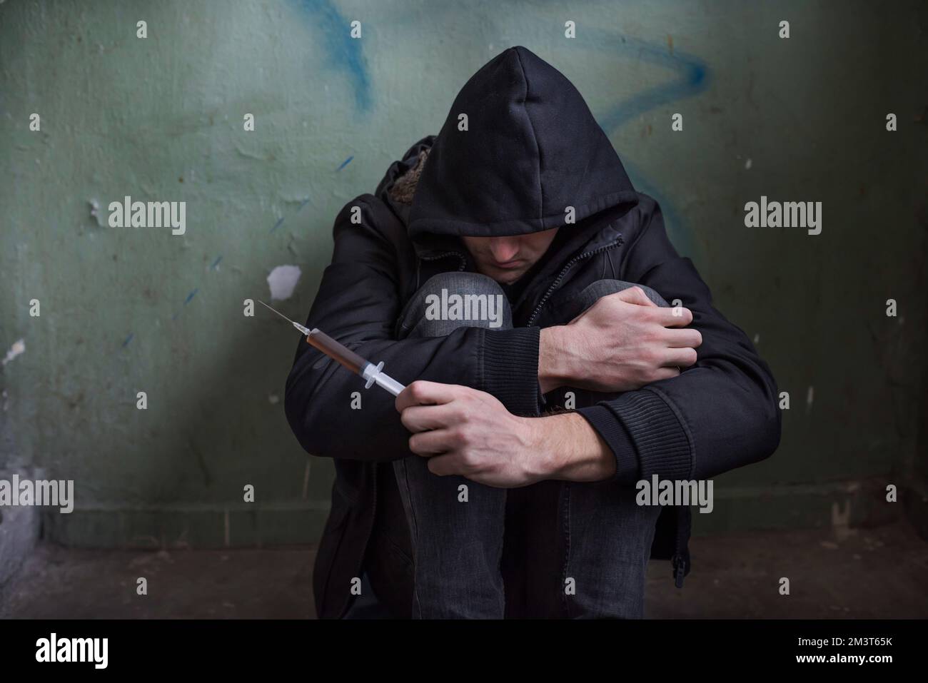 Photo of a desperate young drug addict in the hood and sitting on the ...